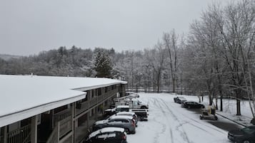 Um estacionamento coberto de neve, com vários carros e um edifício com telhado plano.