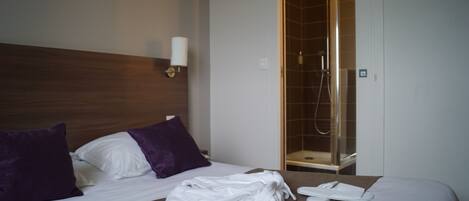 Quarto de hotel com cama, roupão e zona de chuveiro.