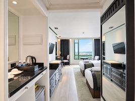 Quarto de hotel com cama, escrivaninha, cadeira, televisão e uma janela grande com vista.