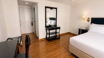 Quarto de hotel com cama, escrivaninha, cadeira, espelho, mesa de cabeceira e abajur.