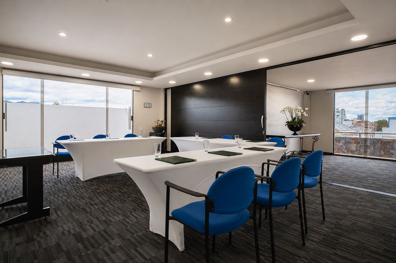 Sala de conferência com uma mesa comprida, cadeiras azuis e grandes janelas com vista.