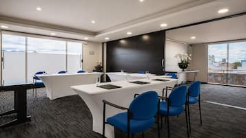 Sala de conferência com uma mesa comprida, cadeiras azuis e grandes janelas com vista.