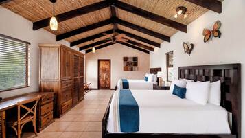 Quarto de hotel com uma cama grande, uma escrivaninha e uma cadeira. Teto de madeira e janela com persianas.