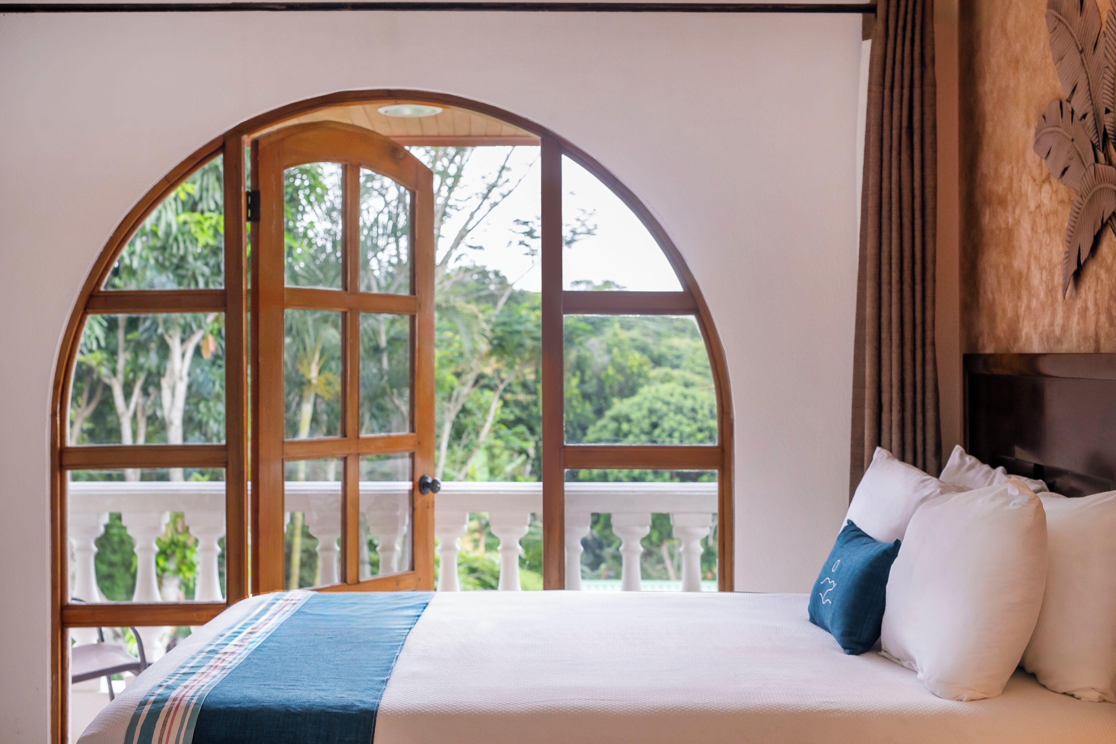 Quarto com uma grande janela em arco, cama com roupa de cama branca e vista para o verde lá fora.