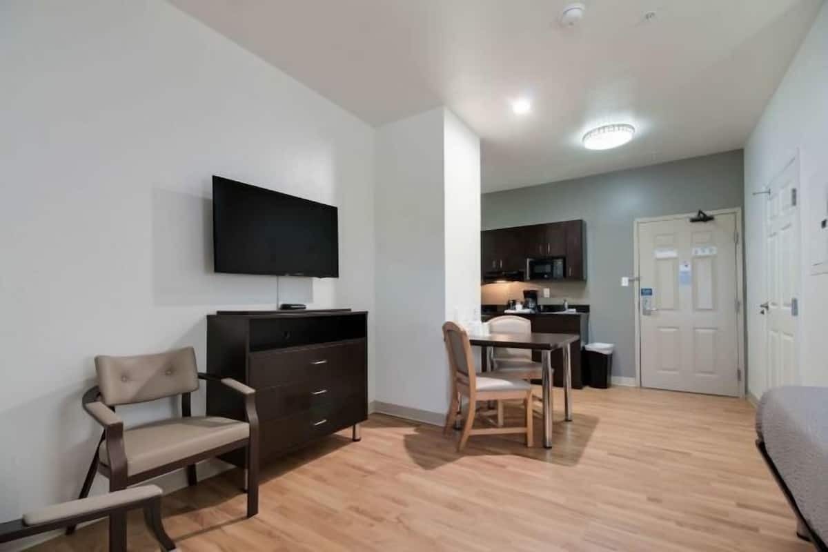 Quarto de hotel moderno com televisão de ecrã plano, secretária com cadeira, cama e kitchenette.