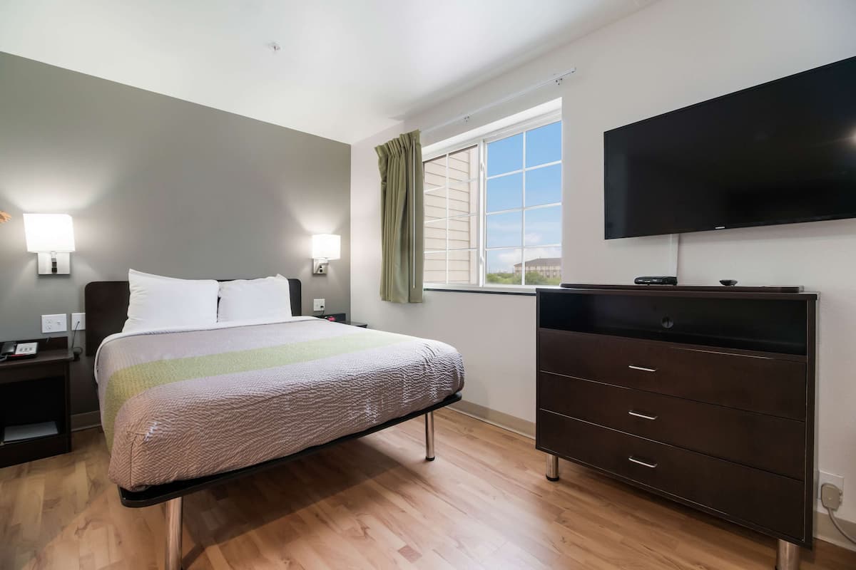 Quarto com cama, luminárias de cabeceira, cômoda e televisão.