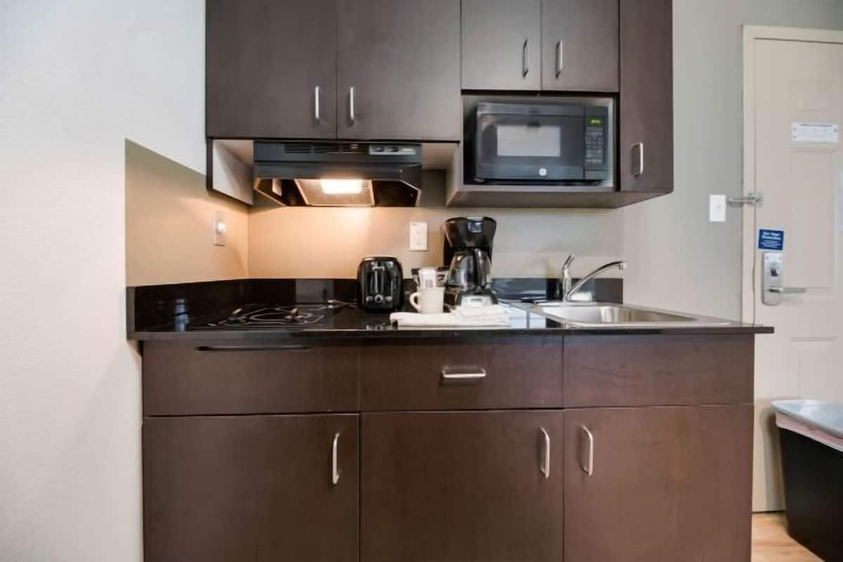 Cozinha compacta com armários escuros, micro-ondas, cafeteira e pia.