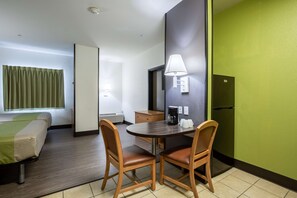 Quarto de hotel com cama, escrivaninha, cadeira, cafeteira e frigorífico.