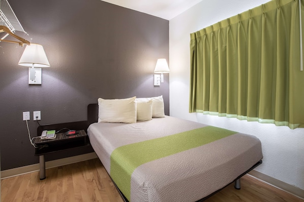 Quarto de hotel com cama, luminárias de cabeceira, mesa de cabeceira e janela com cortinas.