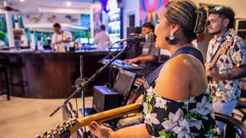 Uma pessoa tocando violão em um bar, com um microfone em frente.