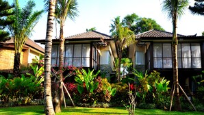 Uma casa de dois andares com telhado de telhas, rodeada por vegetação exuberante e palmeiras.