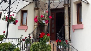 Entrada de hotel com arco de ferro forjado, escadaria e vasos de flores pendurados.