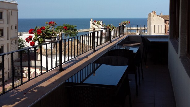 Uma varanda com vista para o mar, uma mesa, cadeiras e plantas em vasos.