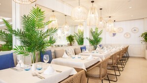 Um restaurante com mesas compridas, cadeiras de vime e luminárias pendentes.