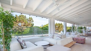 Um espaço amplo e interno, com teto branco, grandes janelas e uma varanda com guarda-corpo de metal.