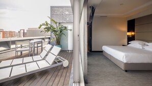 Quarto de hotel moderno com varanda, uma cama e vista para a paisagem urbana.