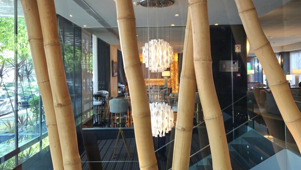 Decoração moderna com colunas de bambu, guarda-corpo de vidro e um lustre central.