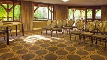 Uma sala de conferências com carpete estampado, várias cadeiras, uma mesa e janelas amplas com cortinas.