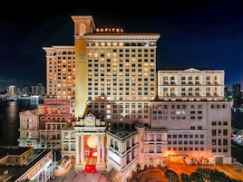 Um hotel grande com vários andares, uma entrada imponente com colunas e vista para o horizonte da cidade à noite.