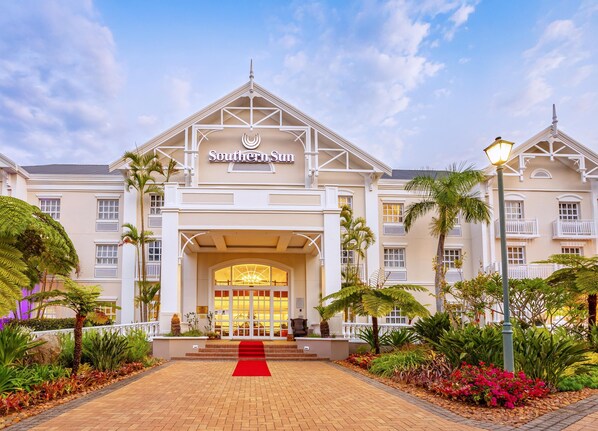 Um hotel com entrada imponente, tapete vermelho e exuberante paisagem tropical.