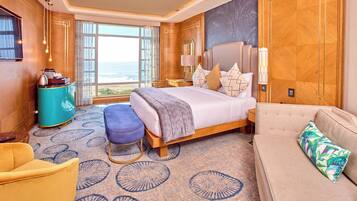 Quarto de hotel com uma cama grande, um sofá, uma mesinha, uma cadeira e vista para o oceano.