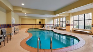 Piscina interior com borda azulejada, áreas de estar e grandes janelas.