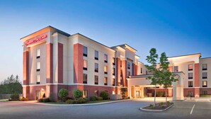Um hotel Hampton Inn & Suites com design moderno, apresentando fachada de tijolos, vários andares e uma entrada bem iluminada.