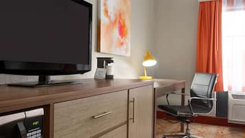 Quarto de hotel com televisão, máquina de café, secretária, cadeira e janela com cortinas.