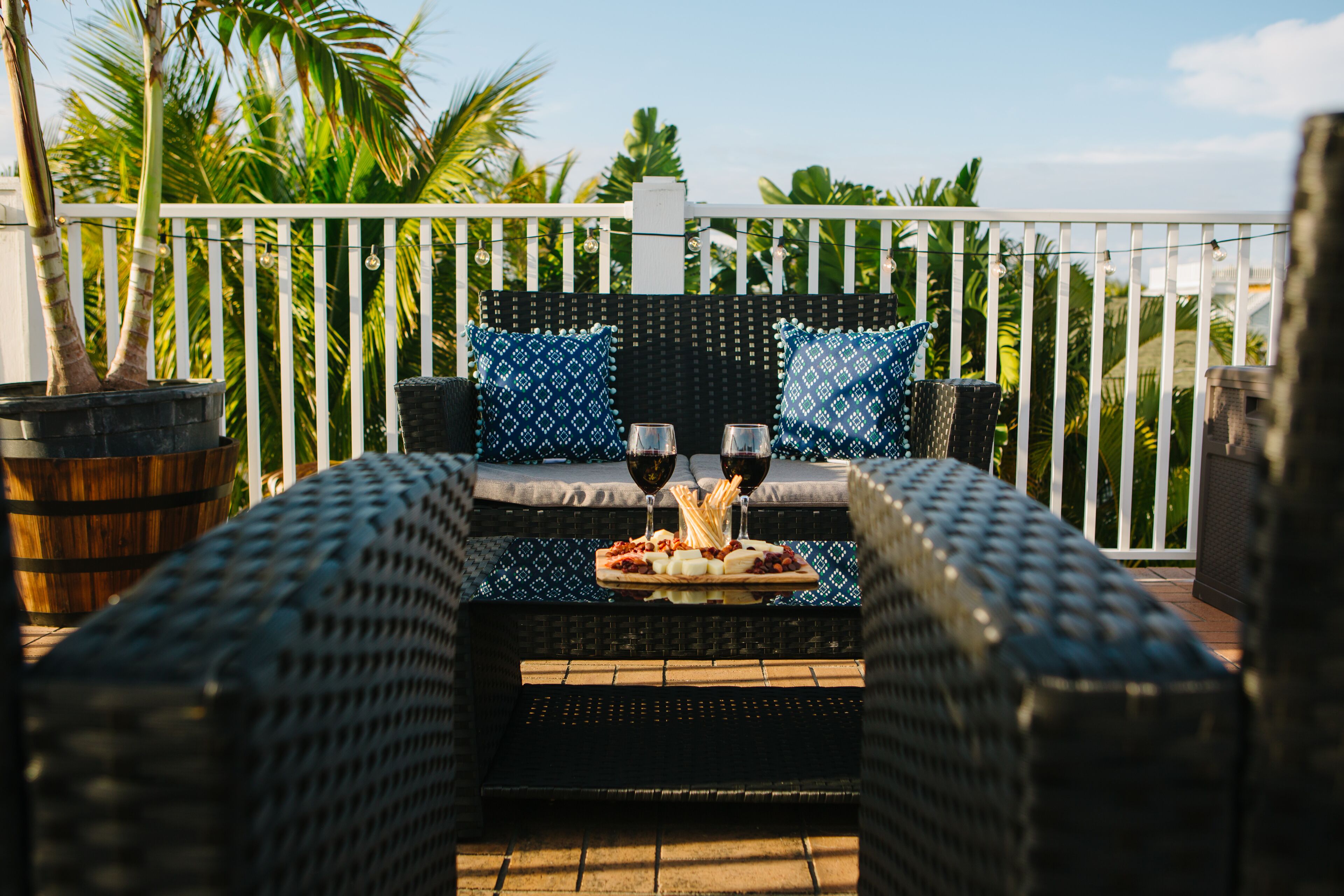 Varanda com móveis de vime, uma bandeja de comida e duas taças de vinho.