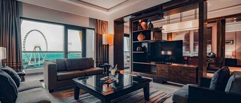 Quarto de hotel moderno com televisão grande, assentos confortáveis, mesa de centro e vista para uma roda gigante.