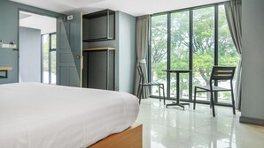Quarto de hotel moderno com uma cama grande, varanda com uma cadeira e vista para árvores.