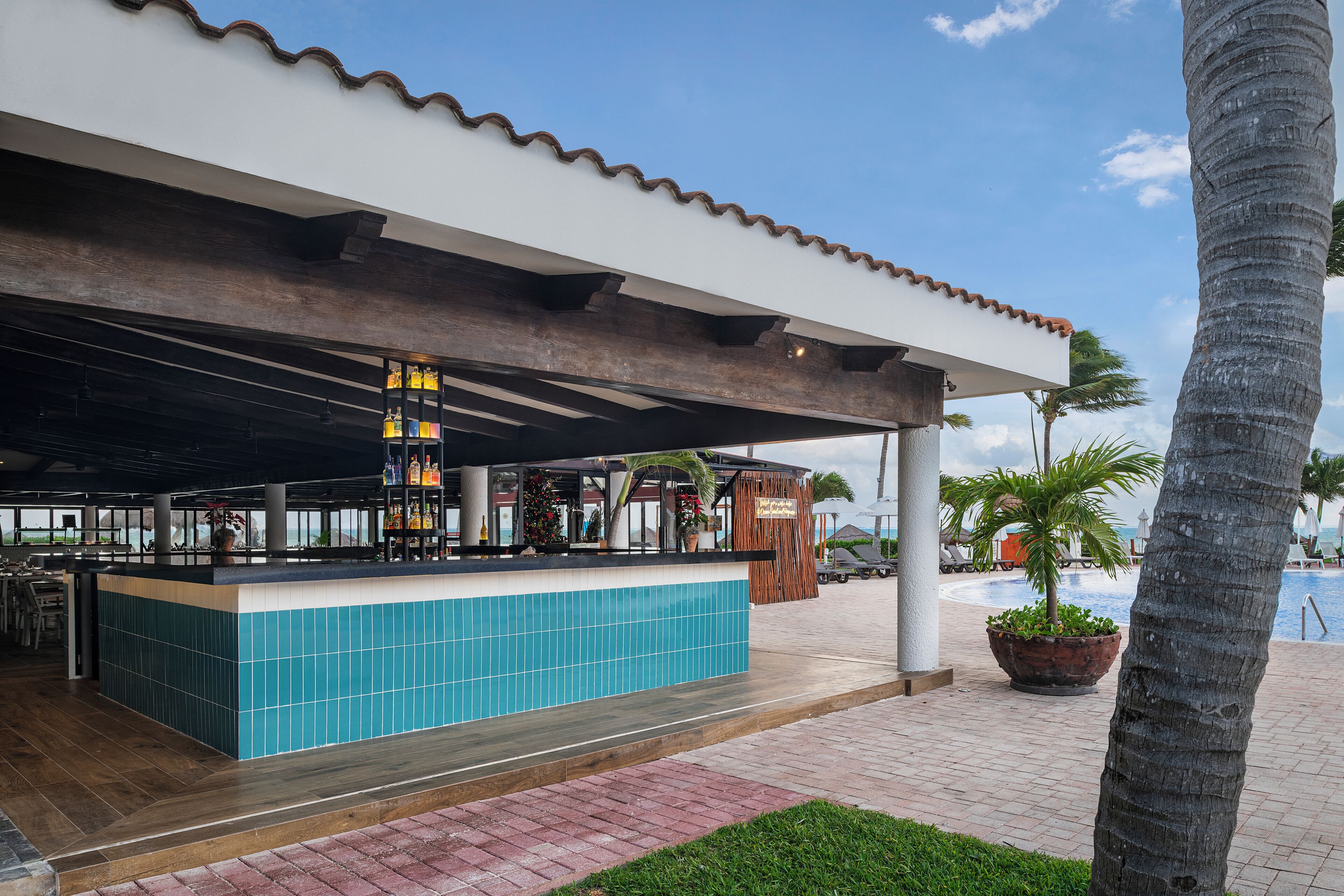 Uma área de bar com balcão revestido de azulejos, mesas ao ar livre e vista para a piscina.