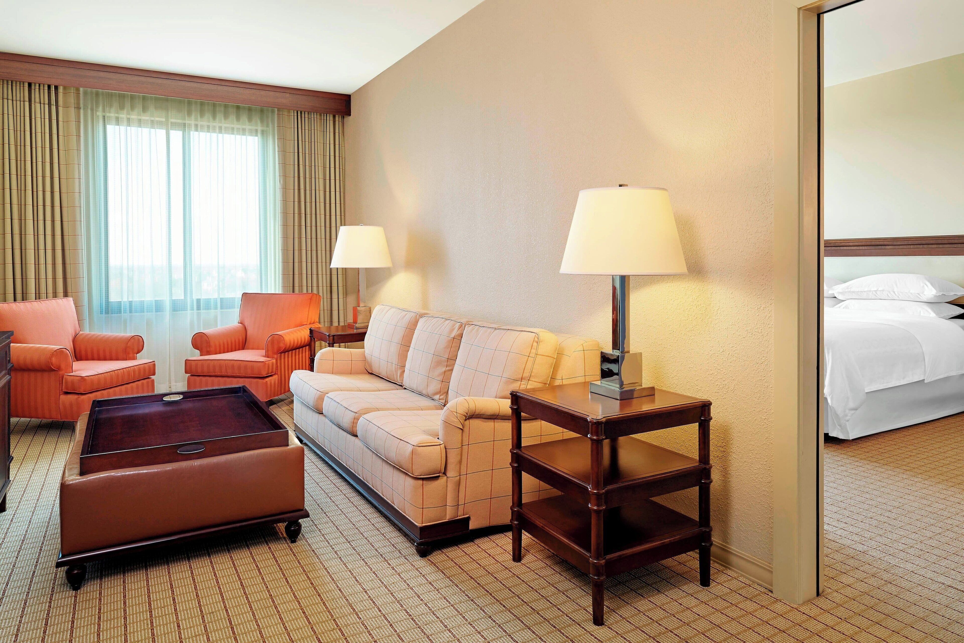 Quarto de hotel com sofá, duas poltronas, mesa de centro, luminária e cama.