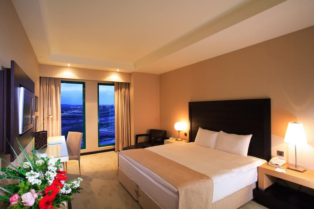 Quarto de hotel com uma cama grande, escrivaninha, cadeira, TV e vista para a paisagem urbana.