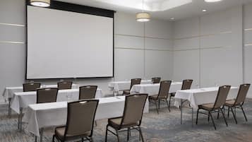 Uma sala de conferência com mesas, cadeiras e uma tela de projetor.
