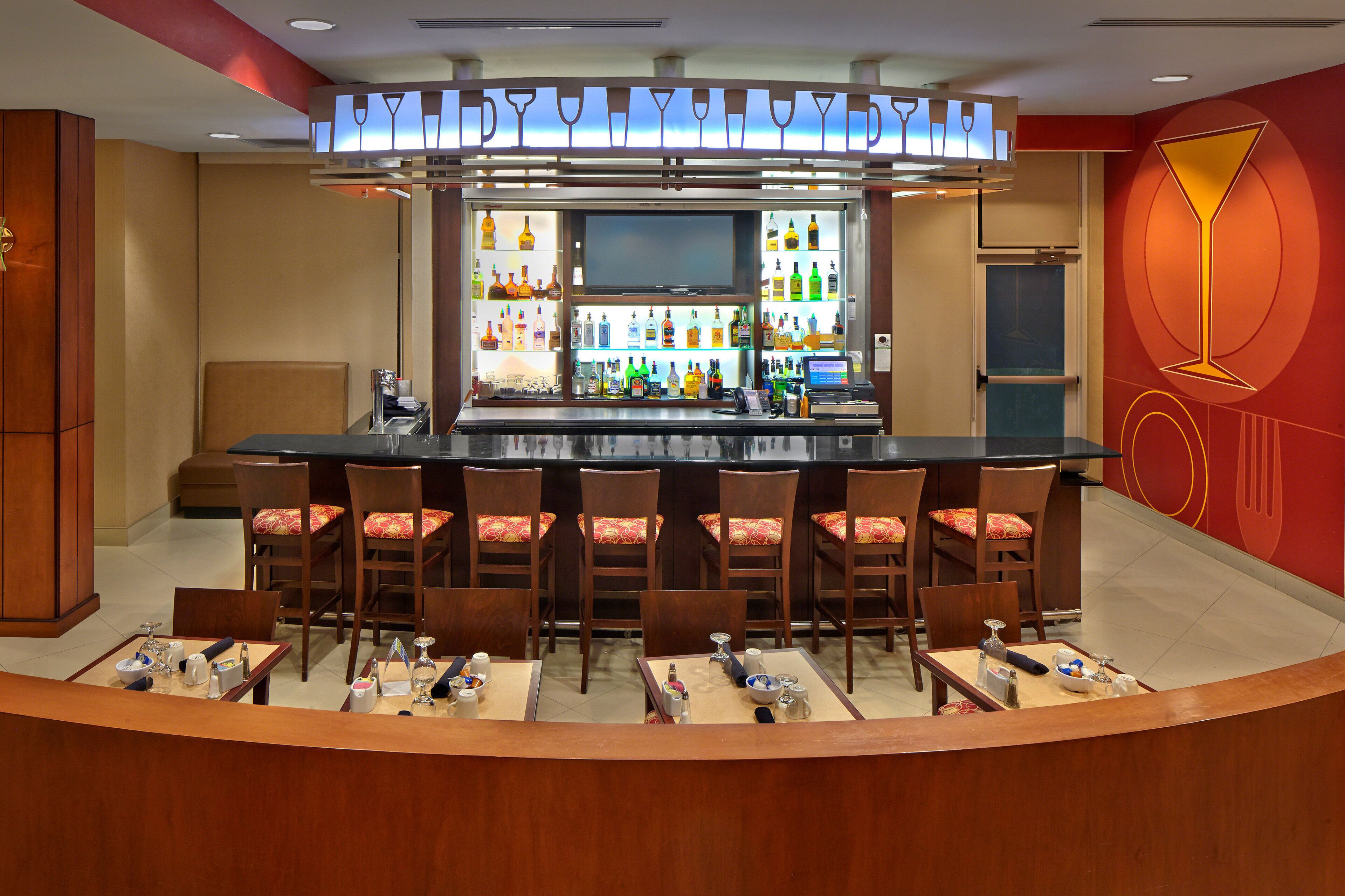 Uma área de bar com balcão, banquetas e diversas garrafas.