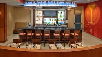 Uma área de bar com balcão, banquetas e diversas garrafas.