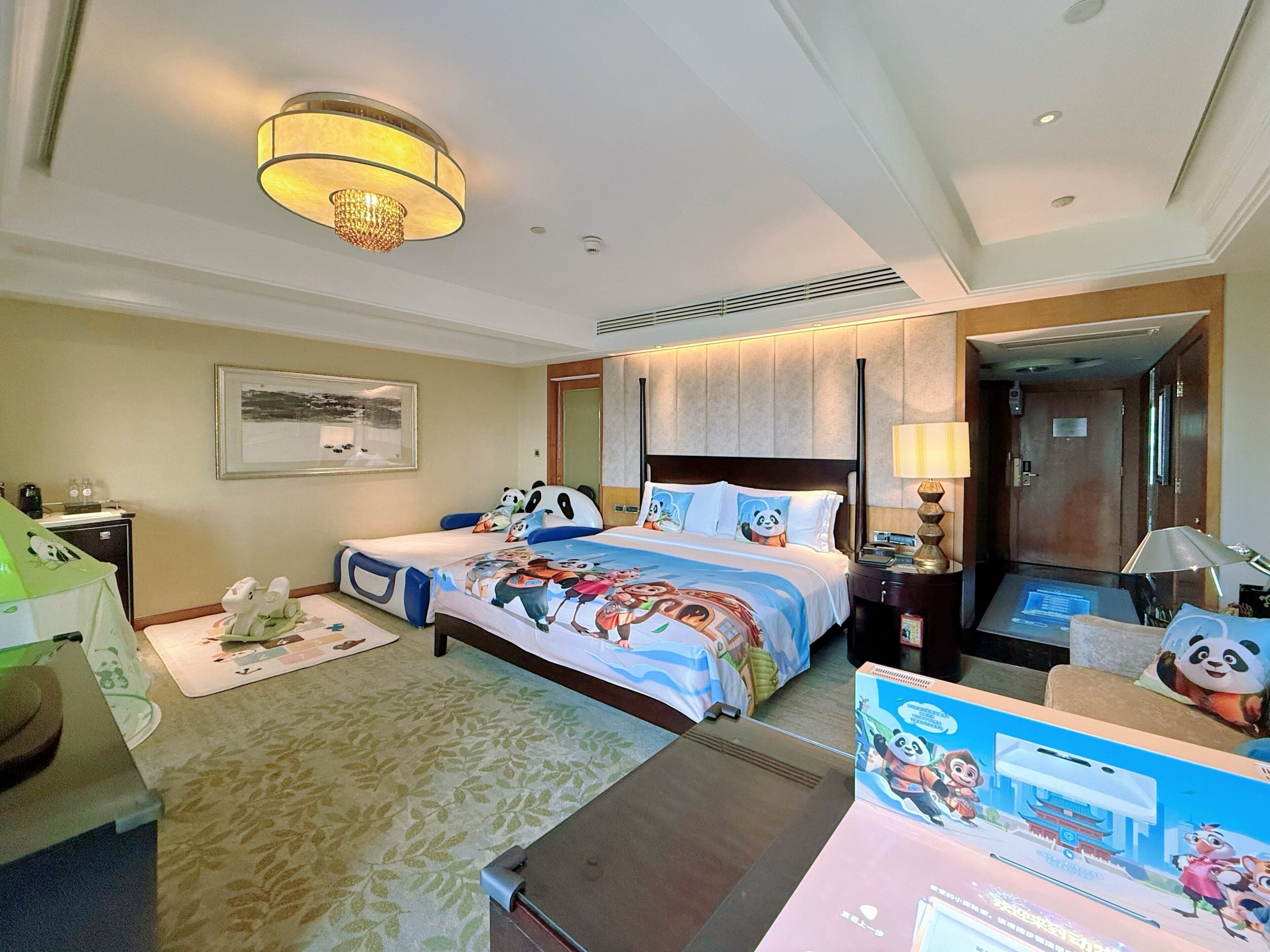 Quarto de hotel com duas camas, uma escrivaninha, uma cadeira, luminária de mesa, quadro na parede e uma janela grande.