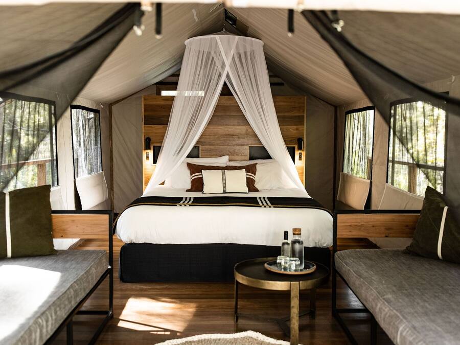 Um quarto tipo tenda com cama de dossel, dois sofás, uma mesinha e janelas amplas.
