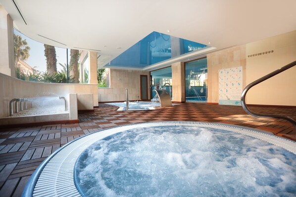 Área de spa com hidromassagem, cadeira de massagem e uma sala envidraçada com vista para palmeiras.