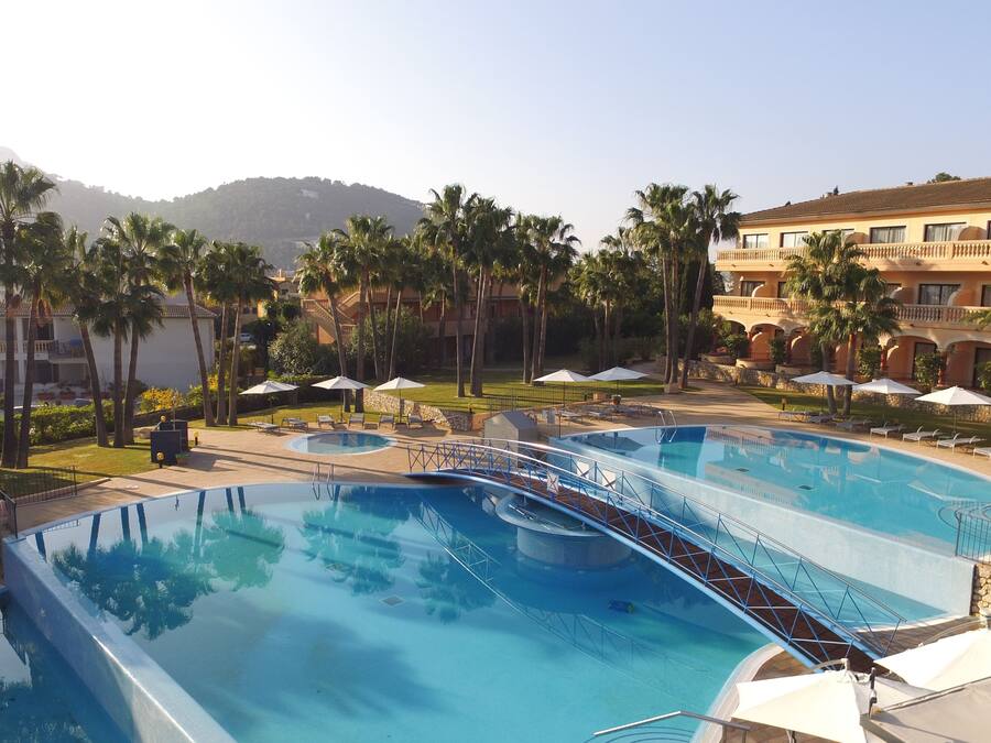 Um resort com uma piscina grande e sinuosa, palmeiras e uma montanha ao fundo.