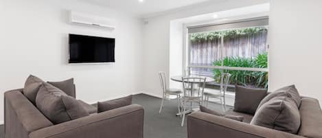 Uma sala de estar moderna com sofá cinzento, TV de tela plana na parede e área de jantar com mesa e cadeiras.