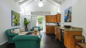 Um quarto espaçoso com teto alto, área de jantar com mesa de madeira, móveis de vime verde e cozinha com armários de madeira e bancada.