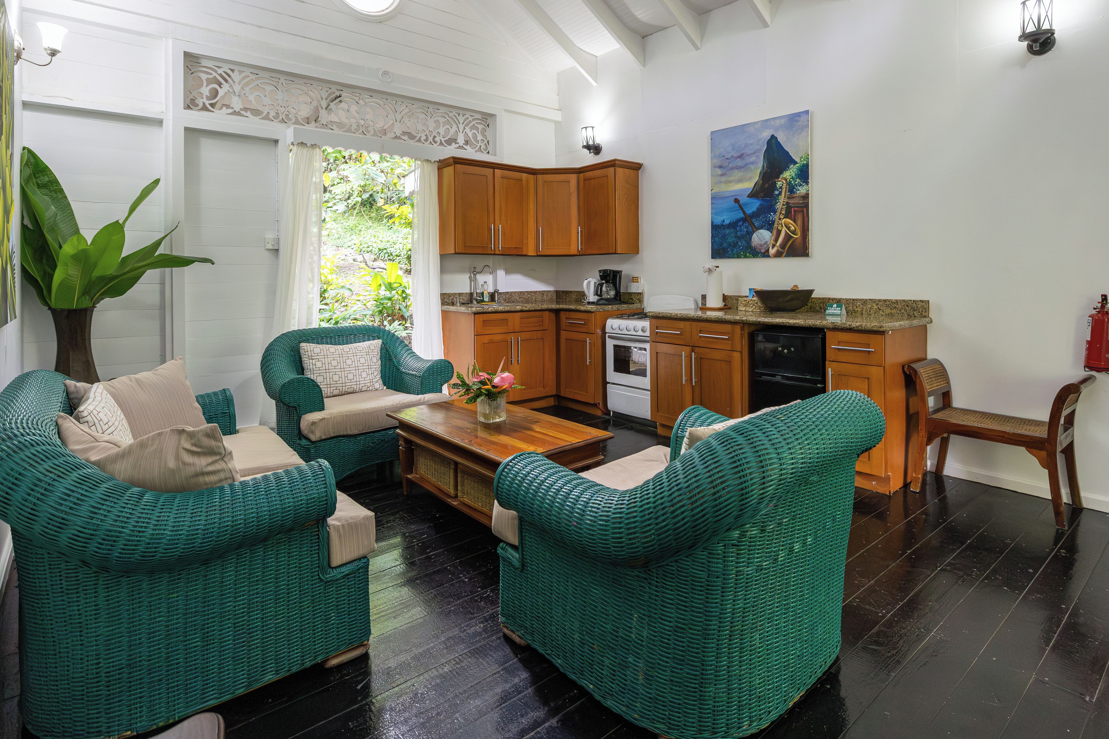 Uma sala de estar com móveis de vime verde, uma mesa de centro de madeira e uma cozinha com armários e eletrodomésticos de madeira.