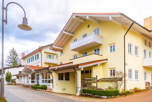 Um edifício amarelo com varanda, um letreiro com a inscrição "Aktiv Hotel Dr. Schweizer" e um poste de luz.
