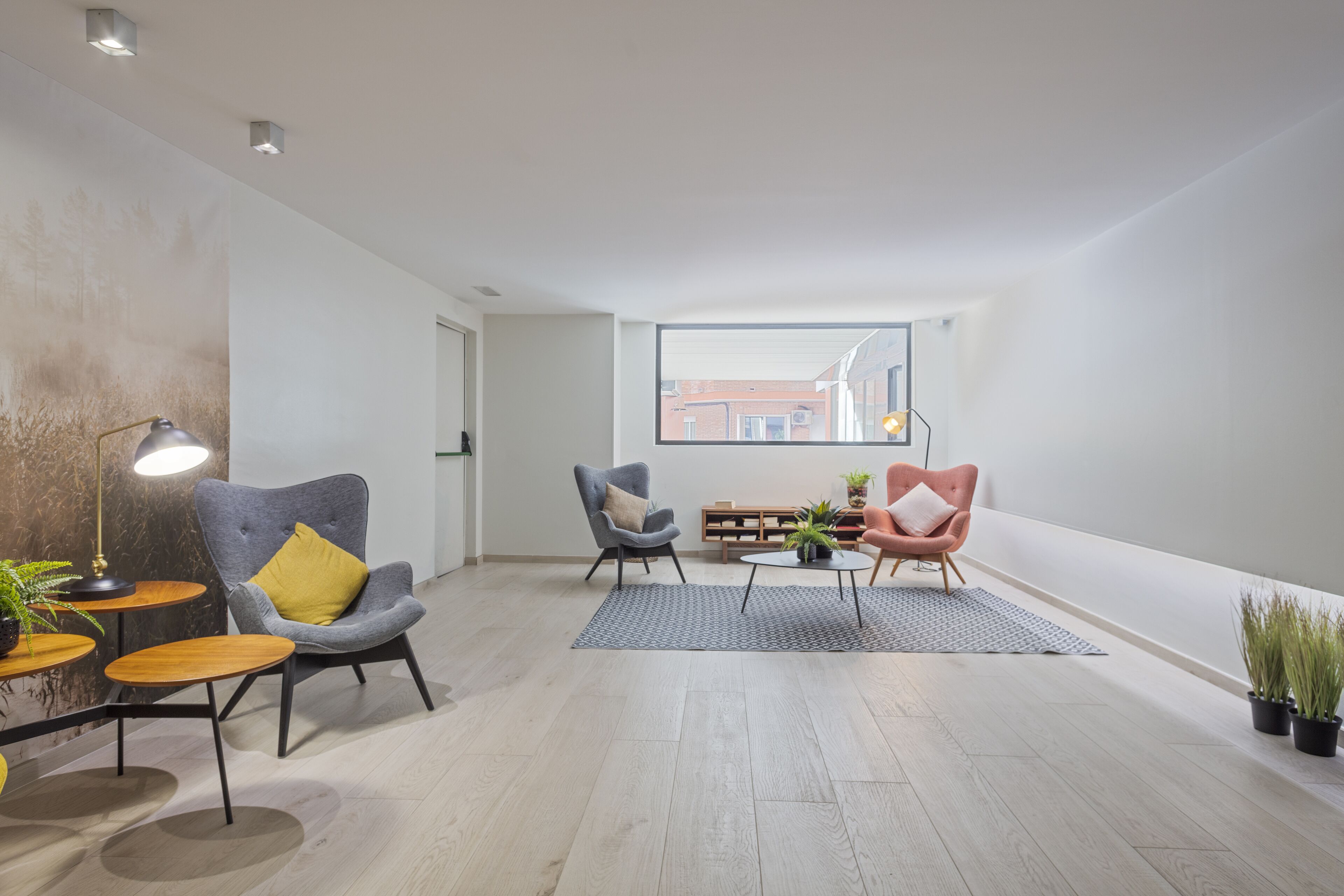 Uma sala de estar moderna com uma janela ampla, duas poltronas, uma mesa de centro e uma estante de livros.