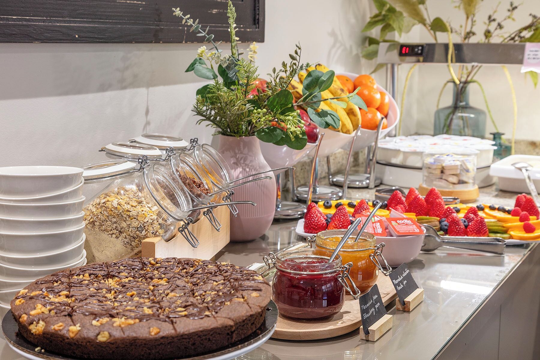Buffet com diversos alimentos, incluindo frutas, um bolo de chocolate e potes com patês.