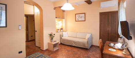 Quarto aconchegante com cama, sofá, mesinha com luminária e porta de madeira.