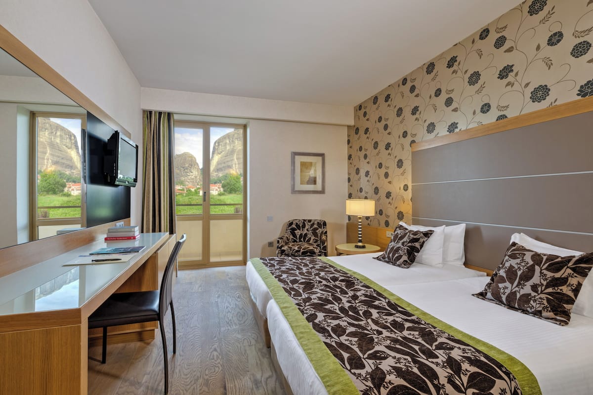 Quarto de hotel com cama, escrivaninha, cadeira, TV e vista para o exterior.