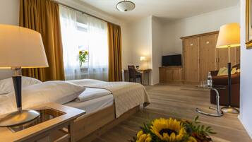 Quarto de hotel com cama, mesa de cabeceira, luminária, televisão, guarda-roupa de madeira e escrivaninha com cadeira.